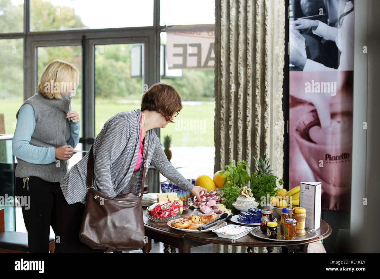 Two women reaching over a table of food in a cafe, UK Stock Photo - Alamy