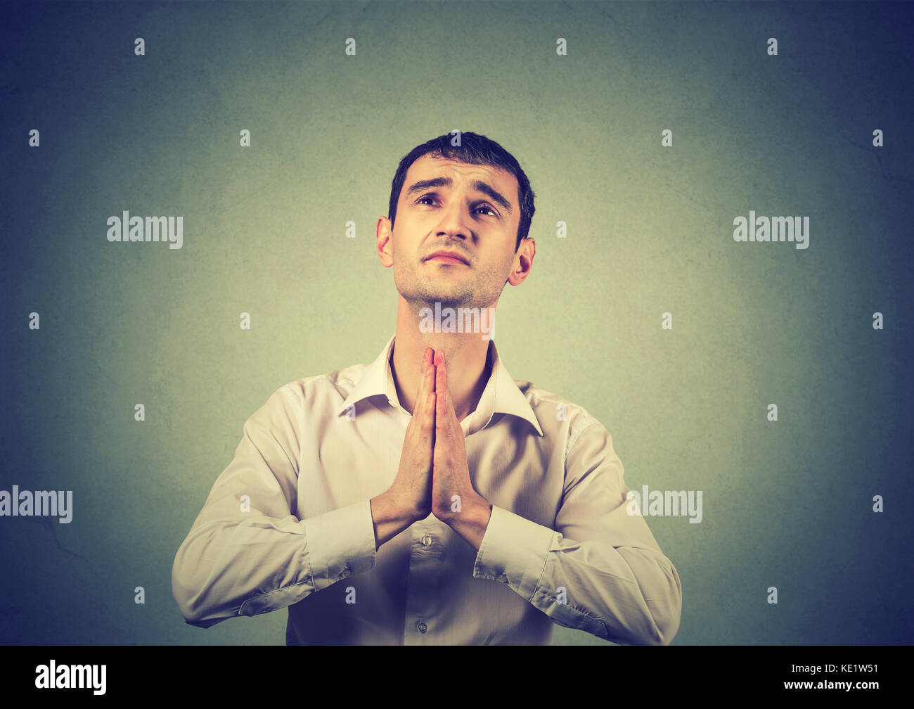 Closeup portrait young man praying hands clasped isolated gray wall ...