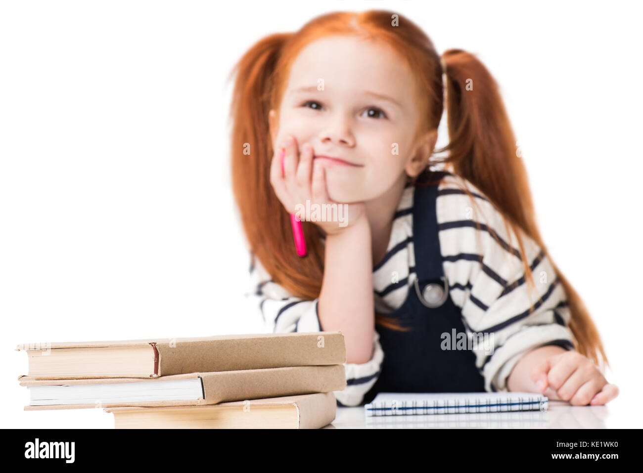 pensive smiling redhead schoolgirl drawing with felt tip pen while ...