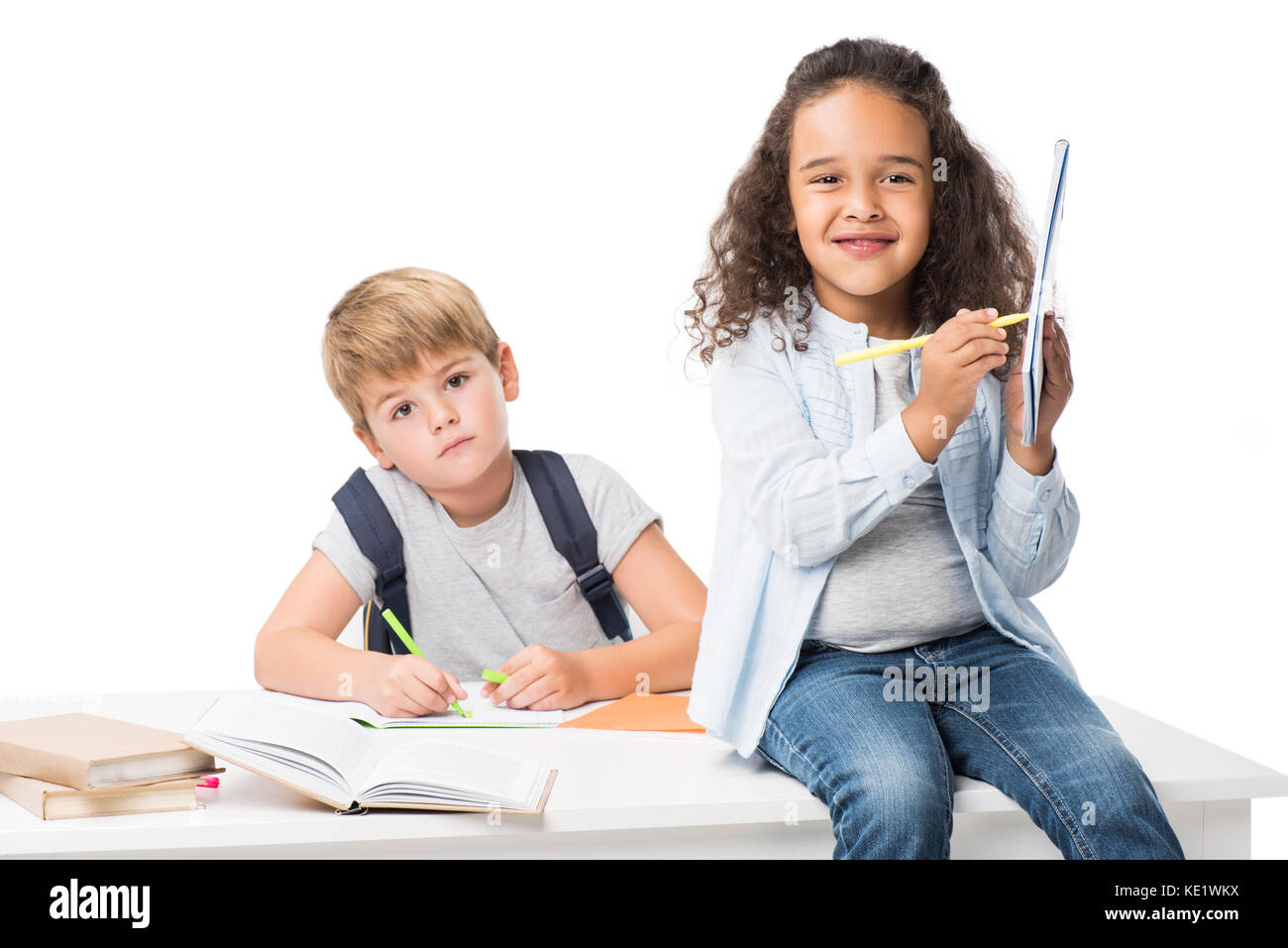 adorable multiethnic schoolkids studying together and looking at camera ...