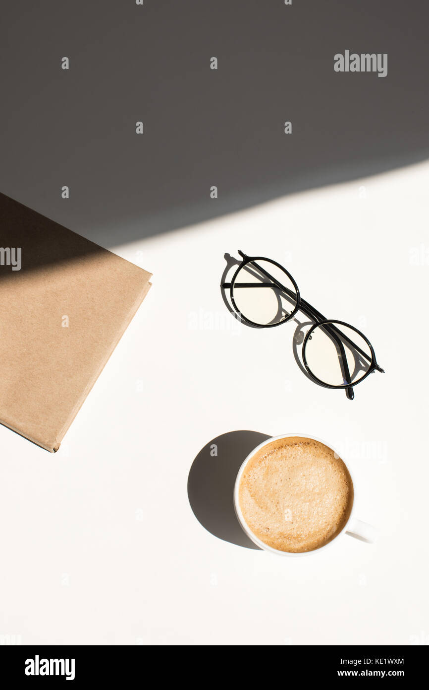 top view of cup of coffee, eyeglasses and notepad on white tabletop ...