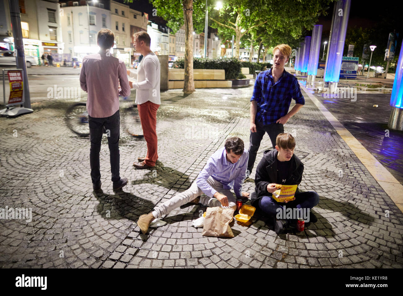 Late night drunk revellers eating takeaways sitting on the floor near ...