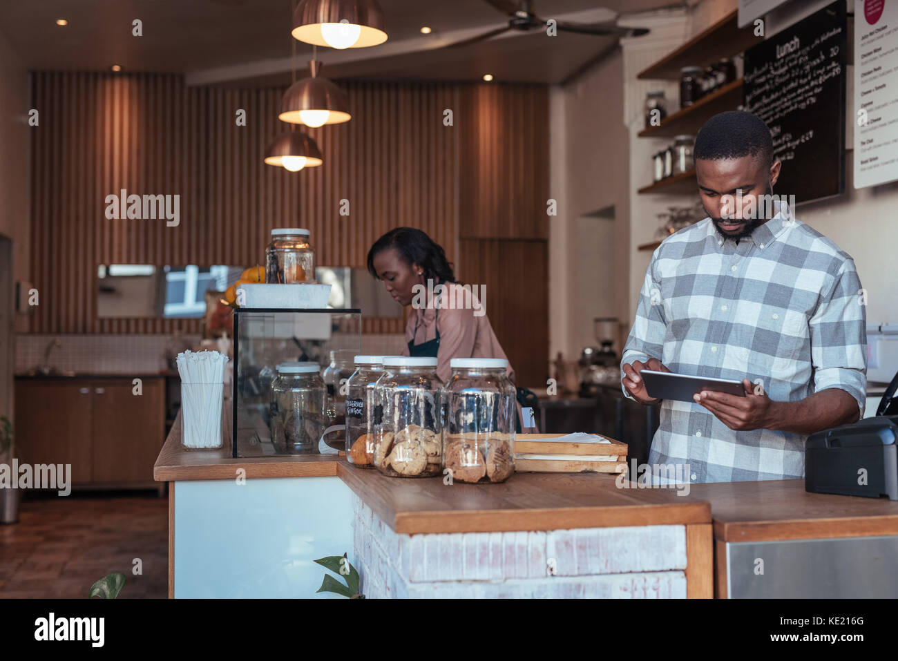 Young African entrepreneur standing behind his cafe counter using a ...