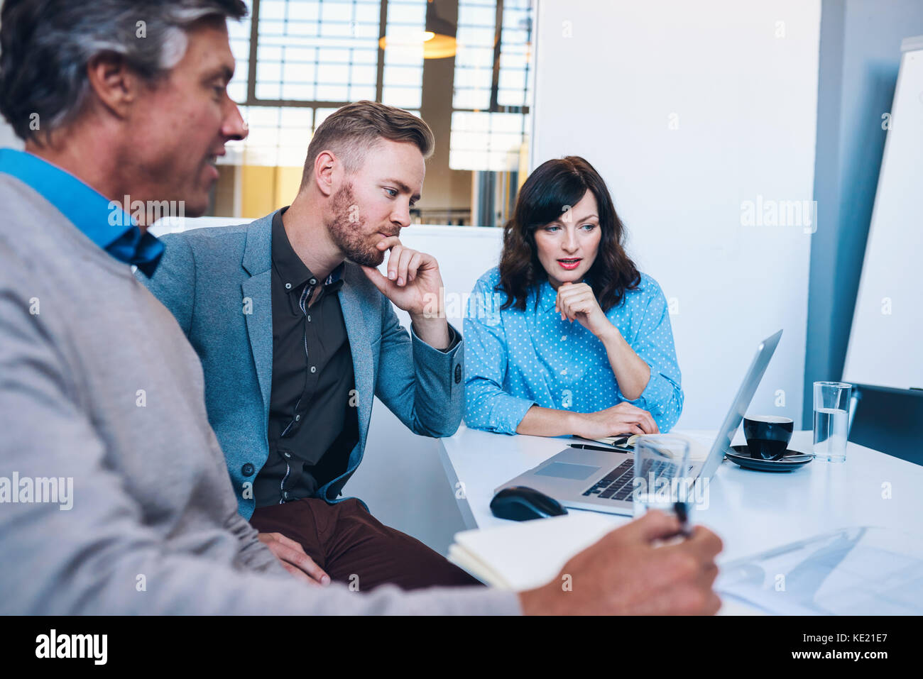Three work colleagues talking and using a laptop together while sitting ...