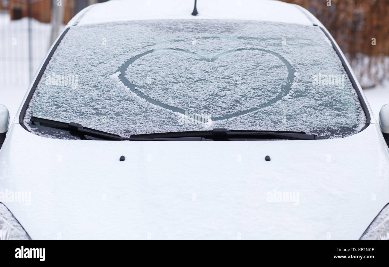 Heart love symbol on windscreen of car in snow. Front view of snowy car ...