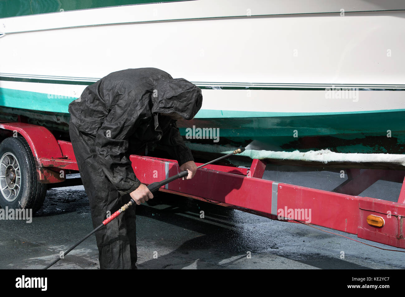 man in black waterproof suit washing boat hull with pressure washer ...