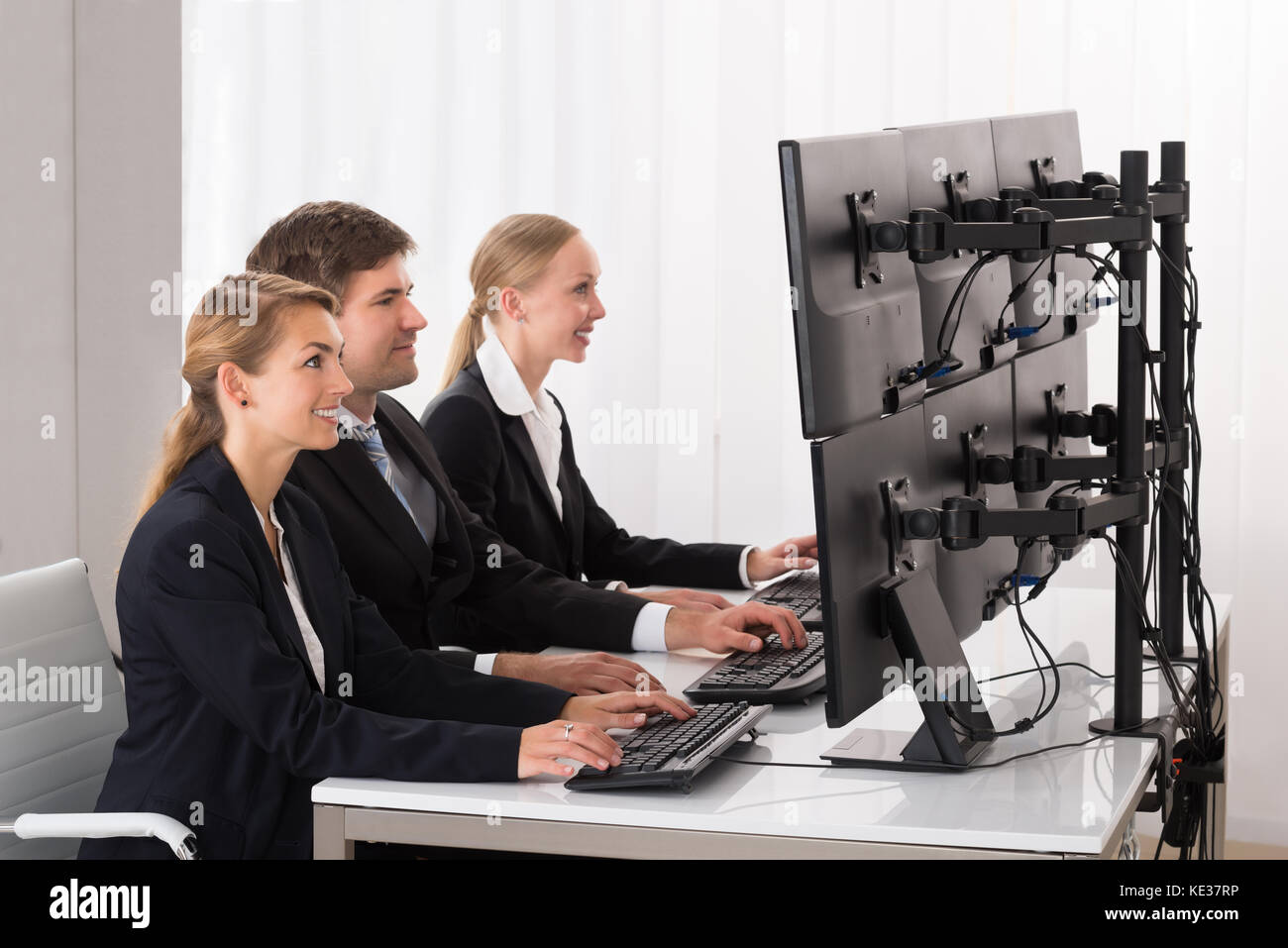 Happy Businesspeople Working On Multiple Computers In Office Stock ...