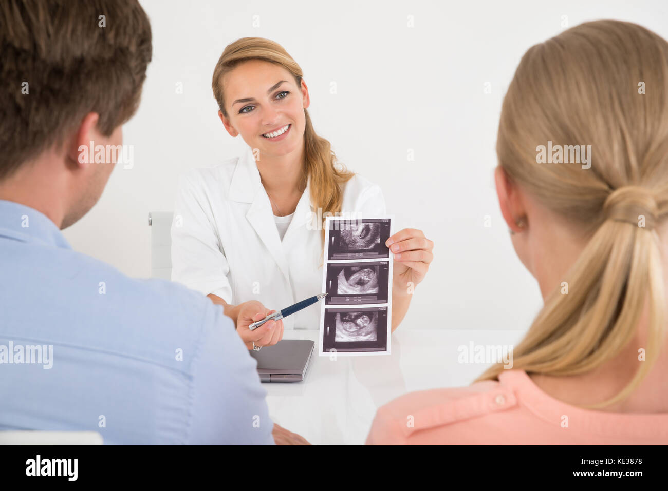Happy Female Doctor Showing Ultrasound Scan To Young Couple In Clinic ...