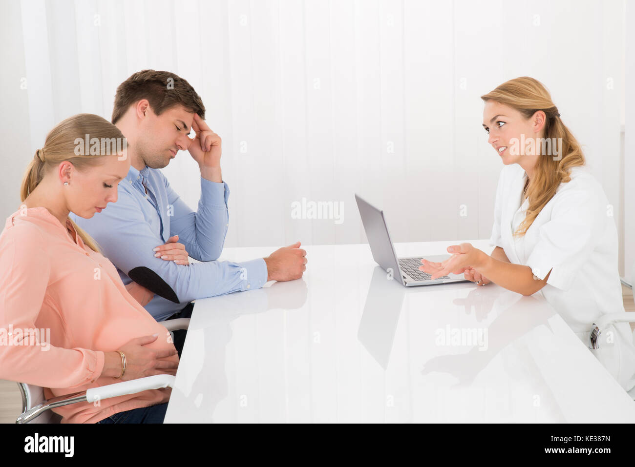Female Doctor Consoling Sad Young Couple Expecting Baby With Laptop On ...