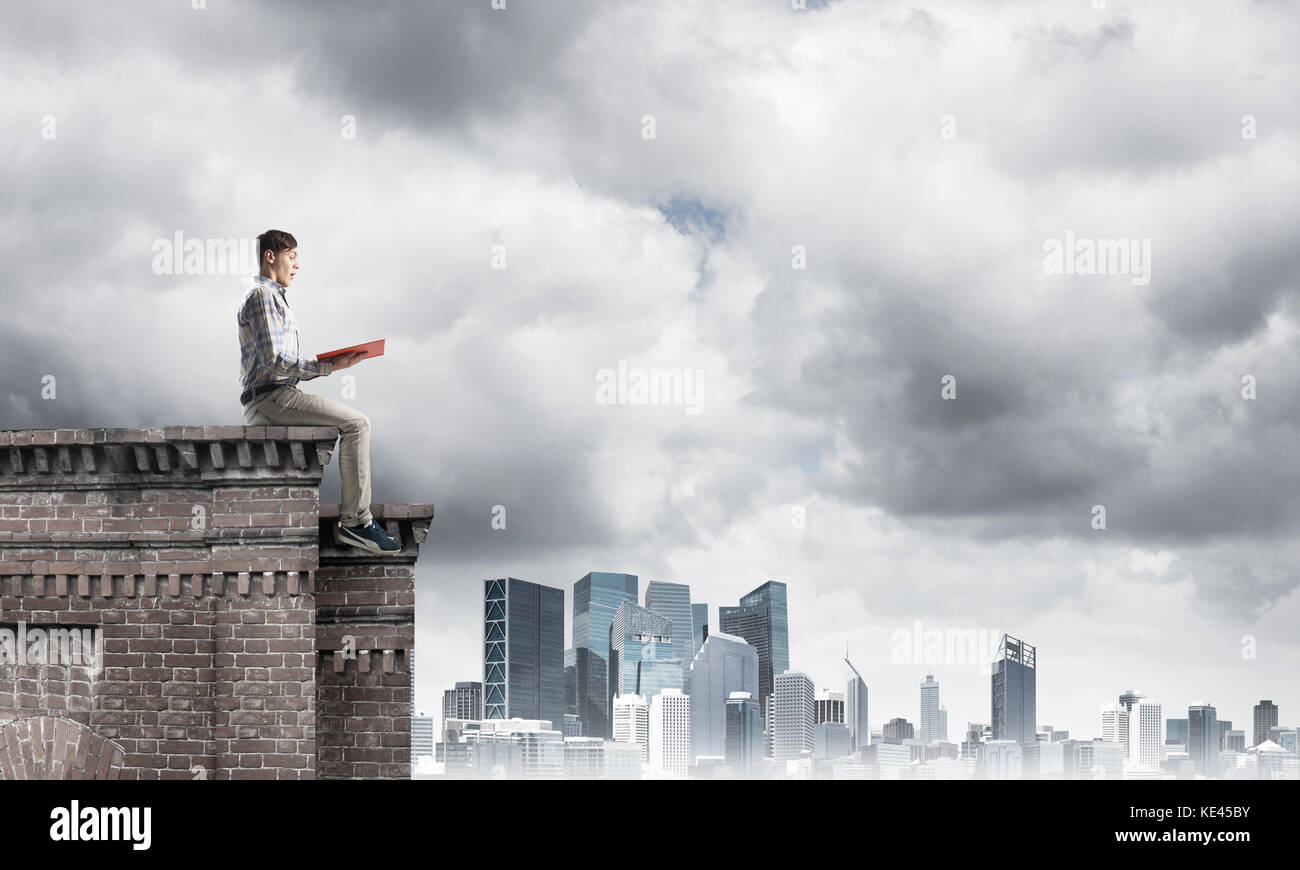 Man on roof edge reading book and cityscape at background Stock Photo ...