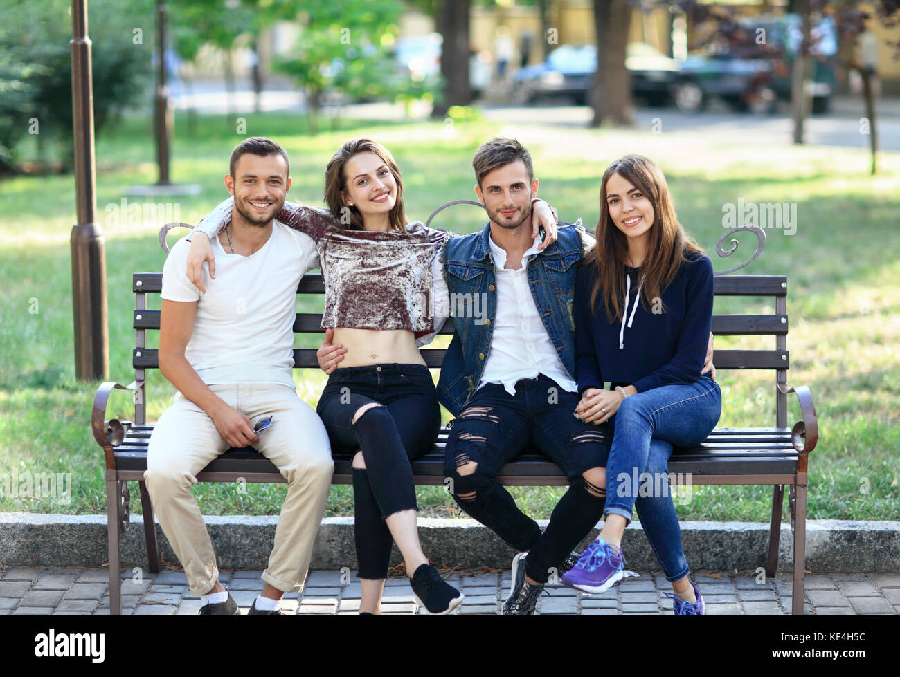 Four women and men sitting on bench in embrace. Happy stylish young ...