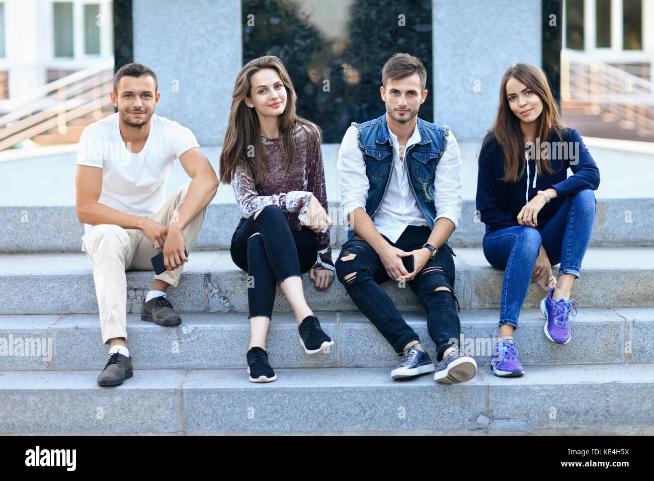 Four young people sitting on stairs outdoors with mobile phones in ...