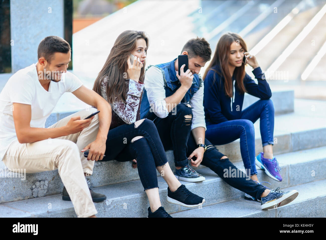 Four young people sitting on stairs and using mobile phones. Two women ...