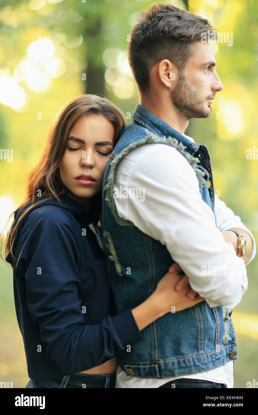 Side view of young woman with closed eyes hugging boyfriend outdoors. Caucasian couple of lovers ...