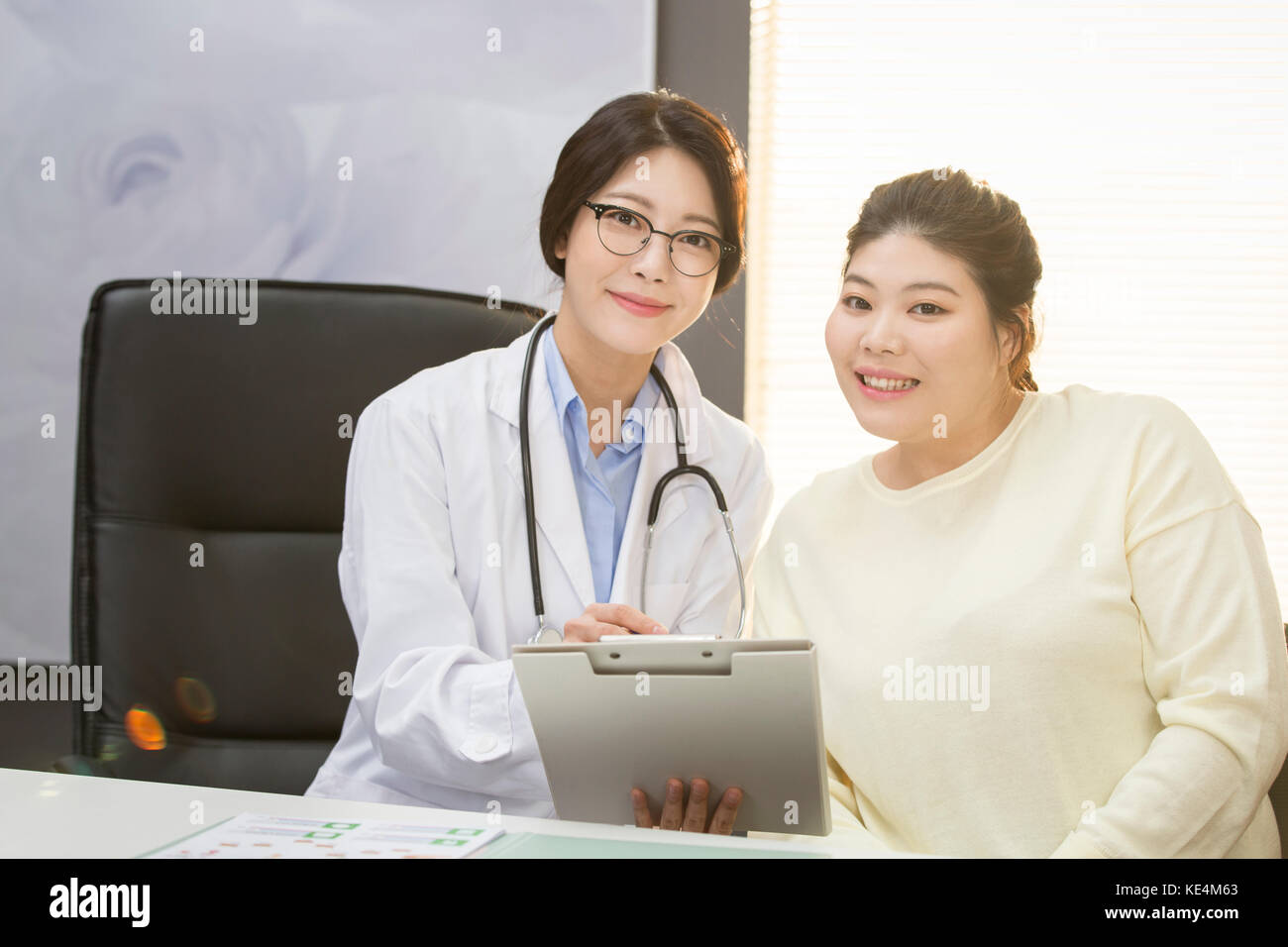 Portrait of smiling female doctor and young fat woman posing at obesity ...
