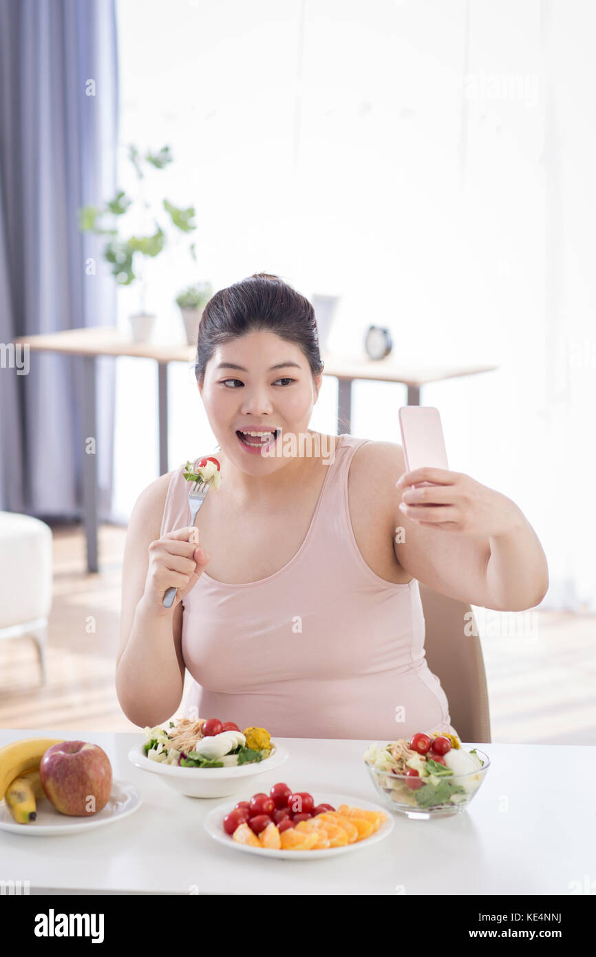 Portrait of young smiling fat woman posing for selfie eating vegetable ...