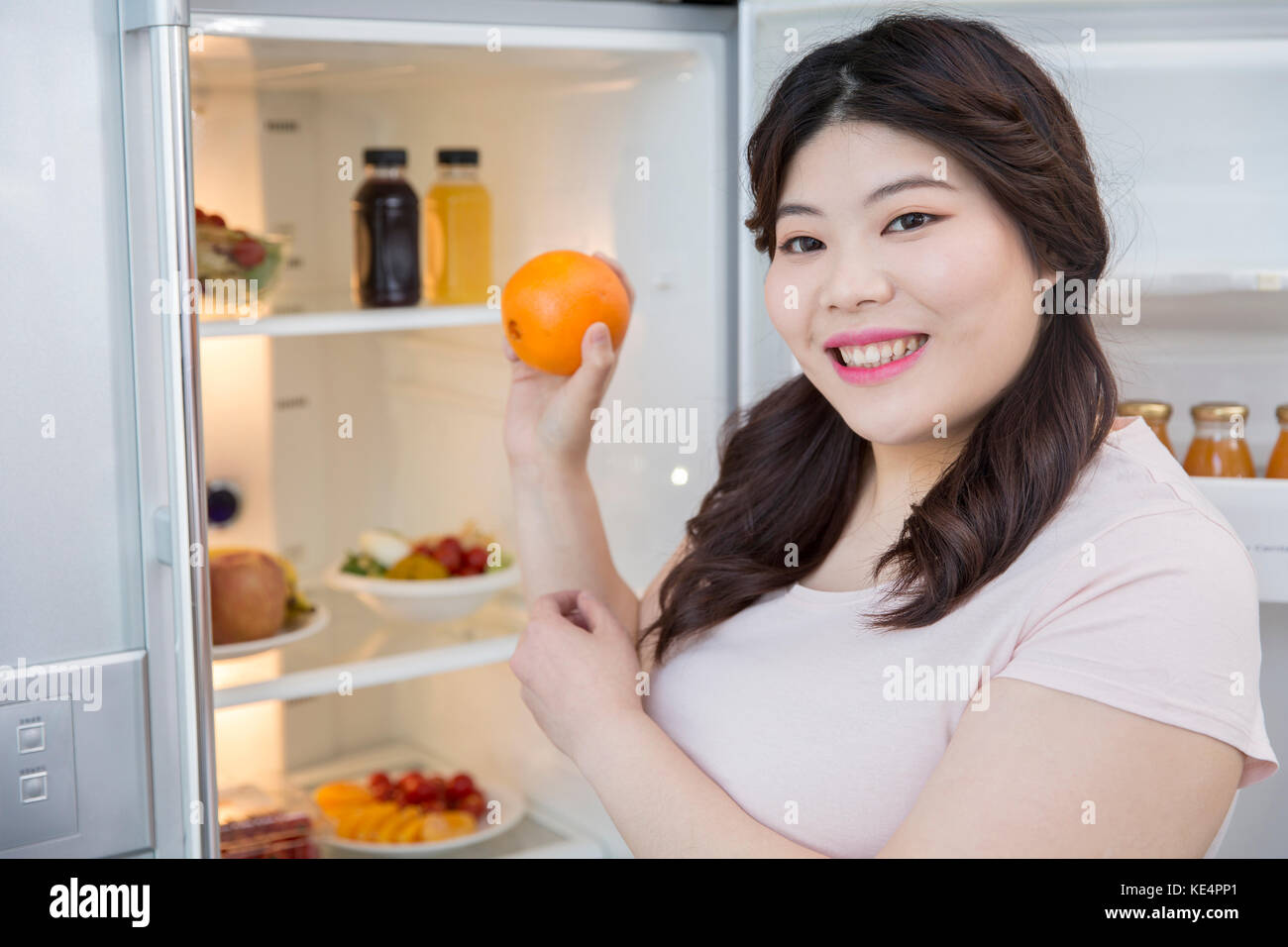 Portrait of young smiling fat woman showing an orange Stock Photo - Alamy