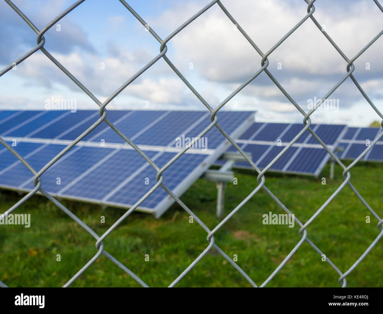 Solar panel or photovoltaic farm behind metal fence on green field with ...