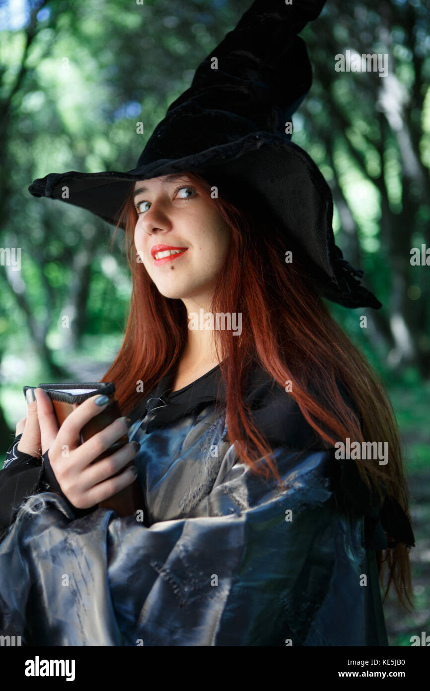 Portrait of witch in black hat and gray cloak holding book of ...