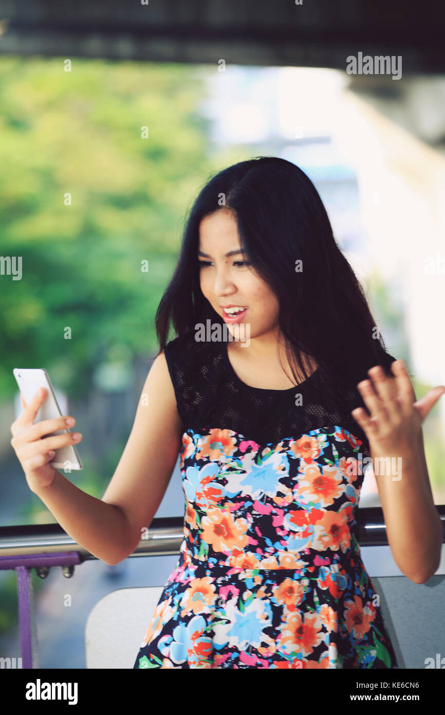 Young Asian woman angry at a text message outdoors Stock Photo - Alamy