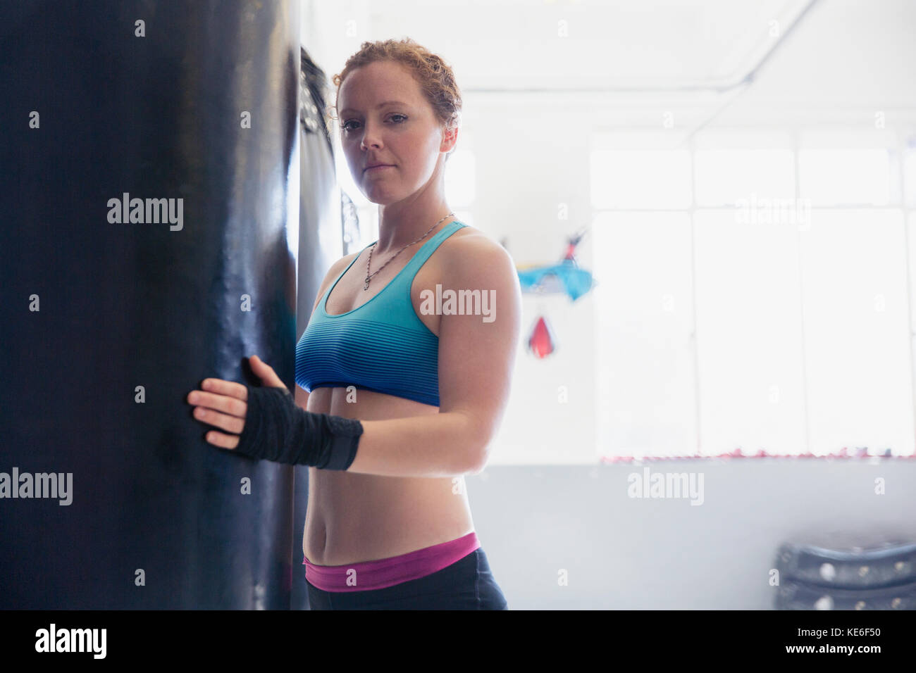 Portrait confident, tough female boxer at punching bag in gym Stock ...