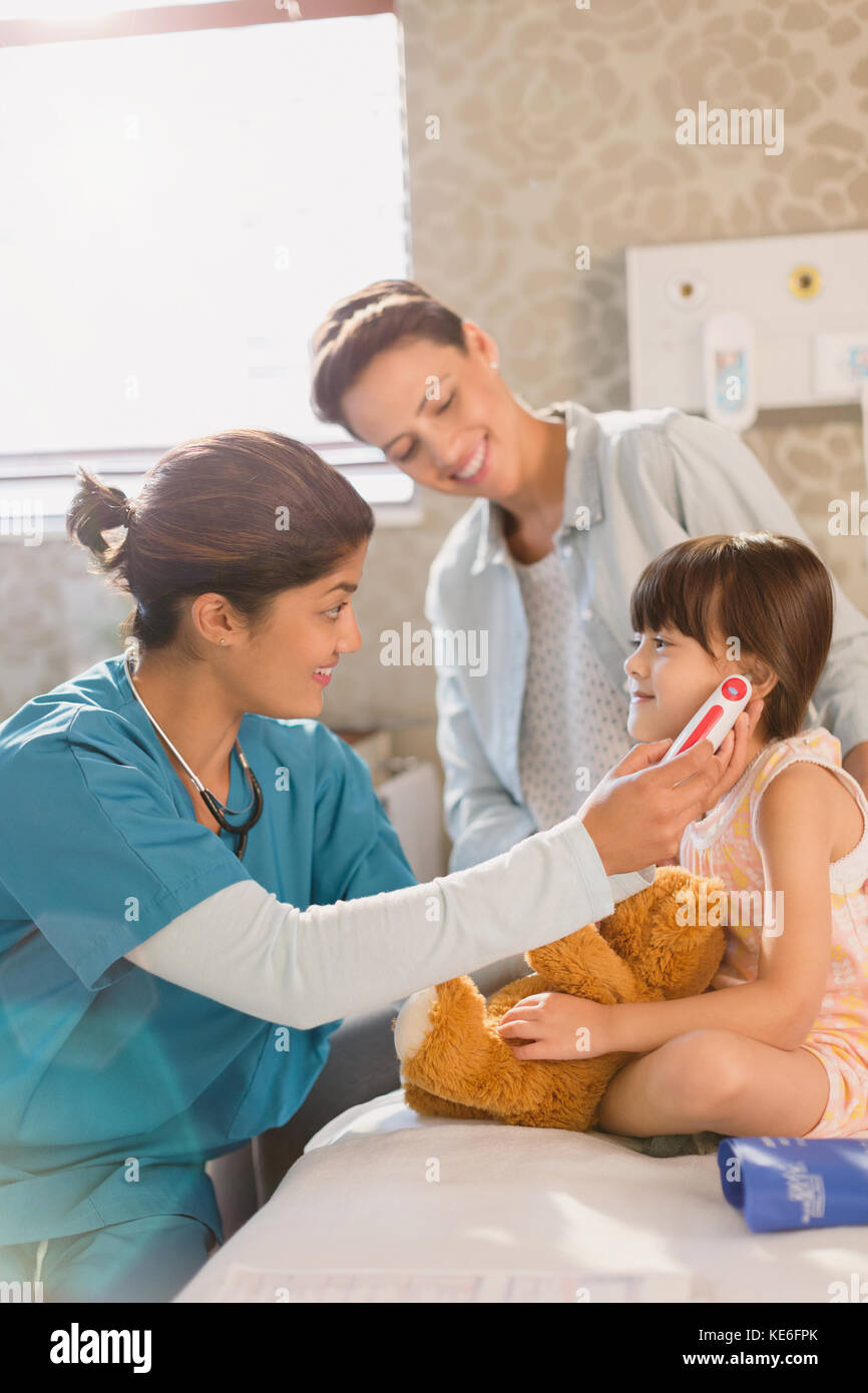 Female nurse using digital thermometer in ear of girl patient in ...