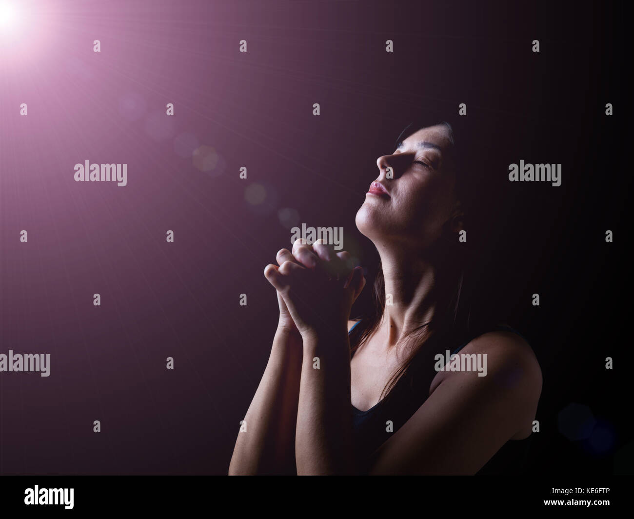 Faithful woman praying under a divine or celestial light and feeling ...