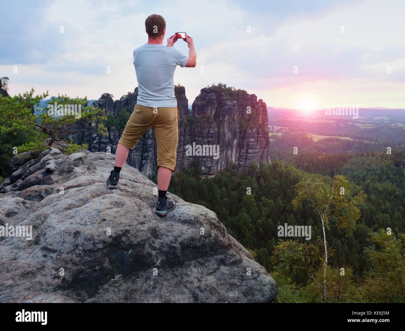 Short hair man on cliff of rock takes photo by smart phone of rocks and ...