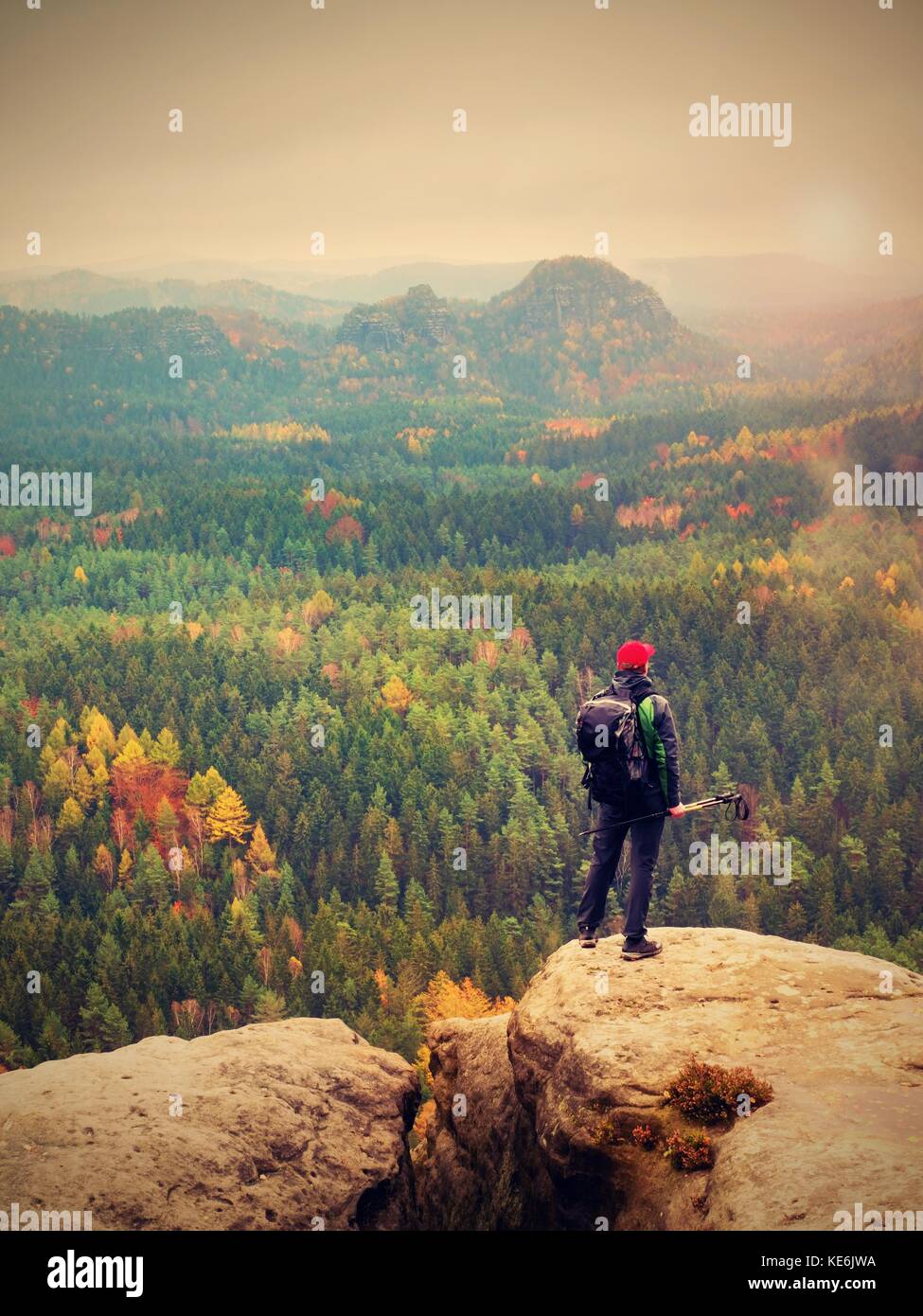 Tall hiker man with red cap, poles in hand and with big backpack stand ...