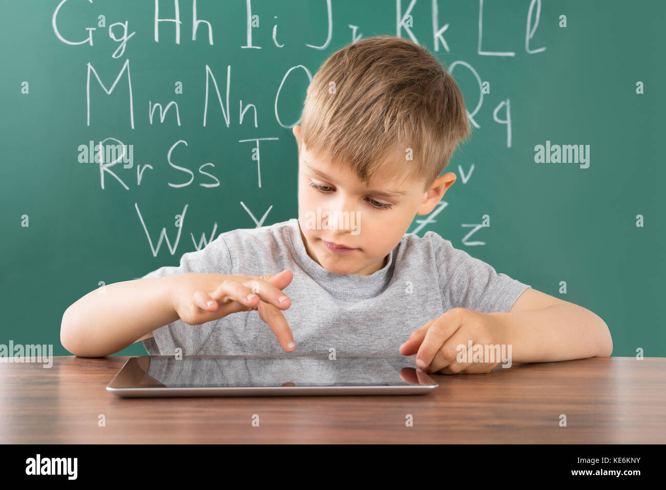Boy Using Digital Tablet In Front Of Green Chalkboard At School Stock ...