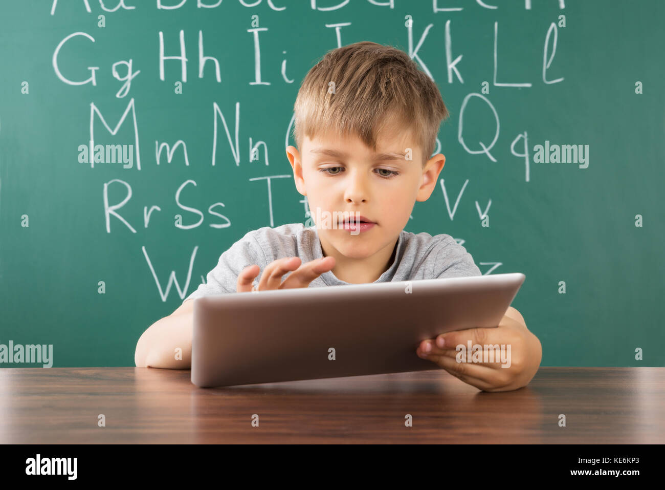 Boy Using Digital Tablet In Front Of Green Chalkboard At School Stock ...