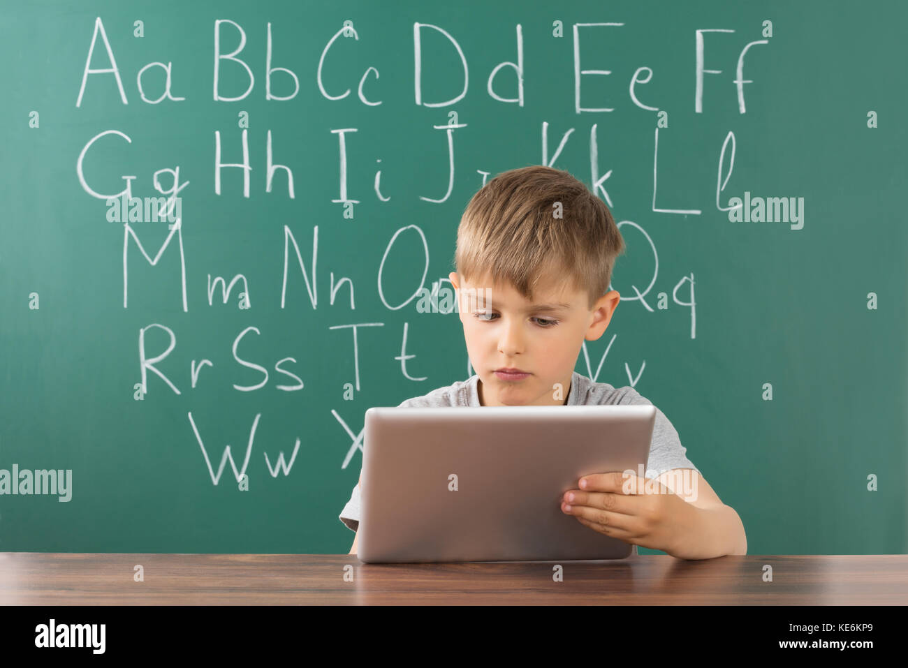 Boy Using Digital Tablet In Front Of Green Chalkboard At School Stock ...