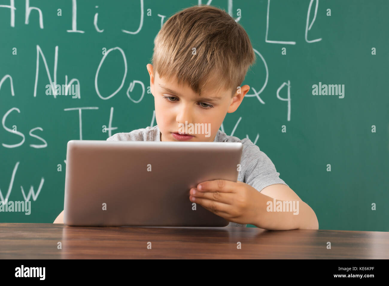 Boy Using Digital Tablet In Front Of Green Chalkboard At School Stock ...