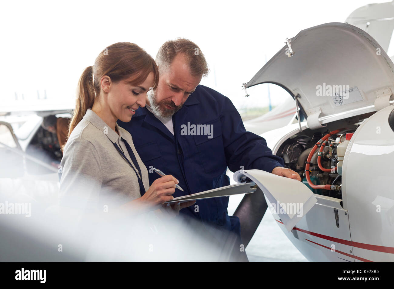 Engineer mechanics reviewing paperwork next to airplane in hangar Stock ...