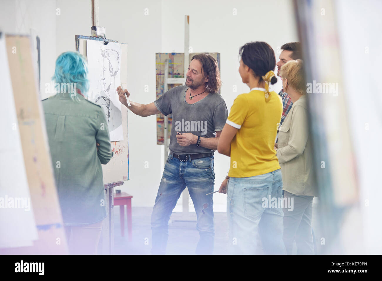 Students listening to instructor sketching at easel in art class studio ...