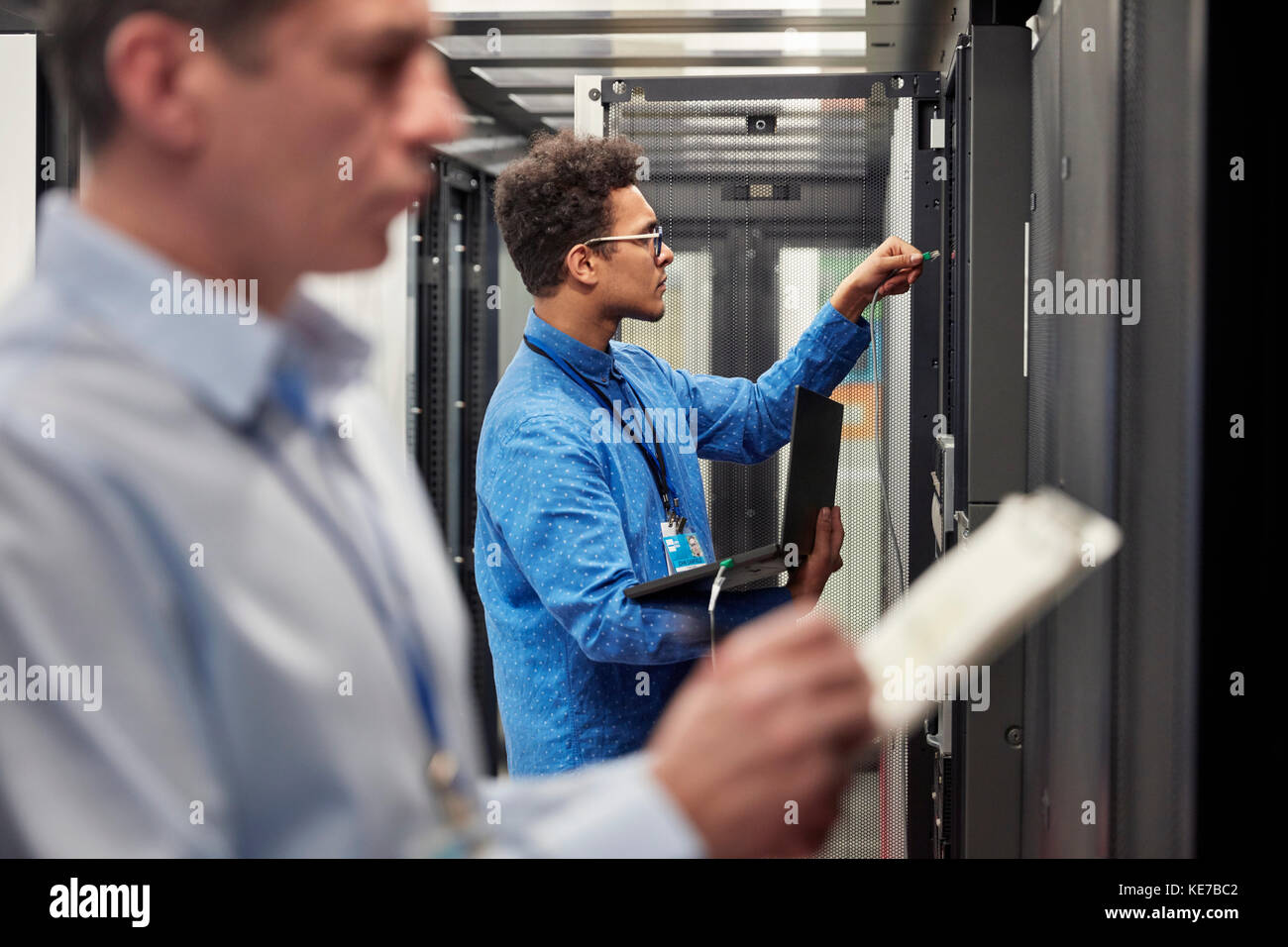 Male IT technicians with clipboard and laptop working at panels in ...