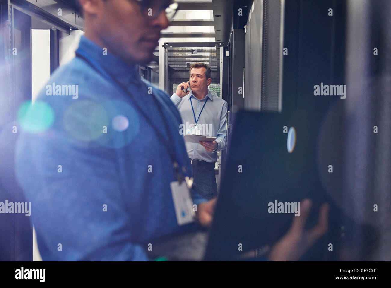 Male IT technicians using laptop and talking on cell phone in server ...