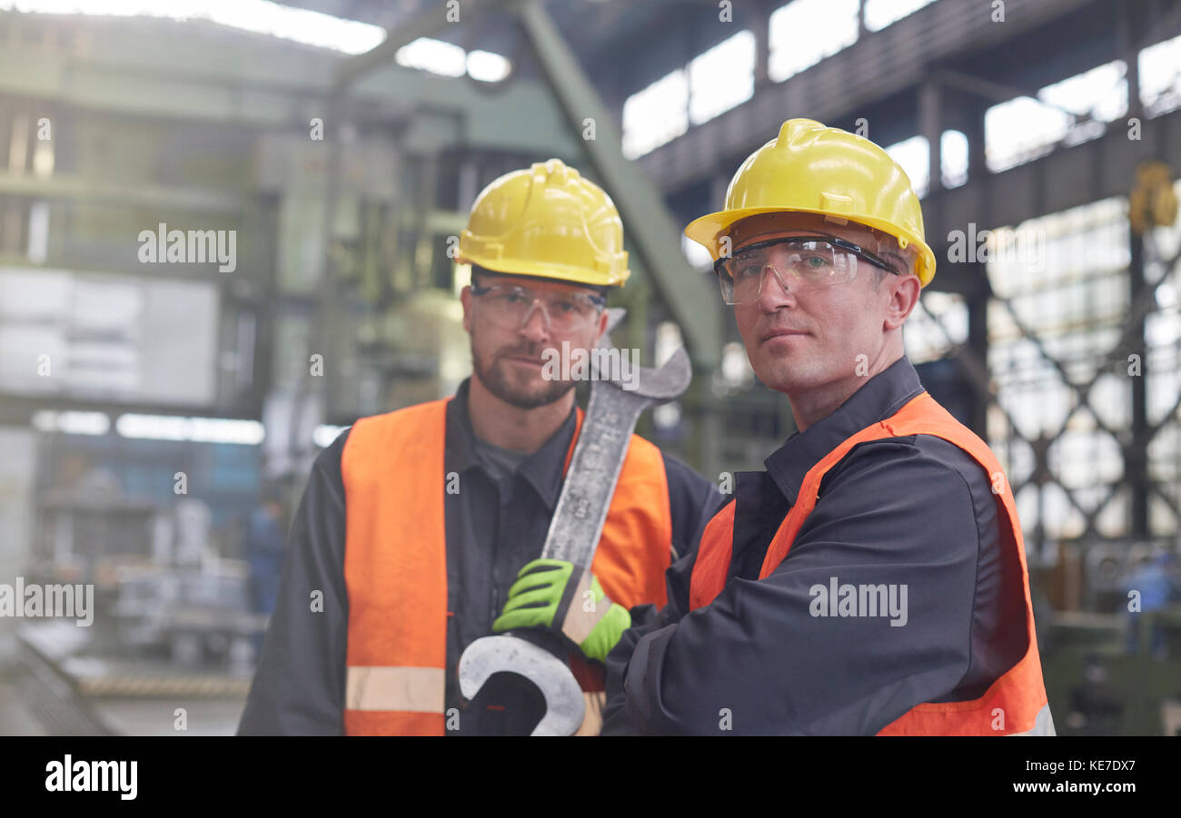 Portrait confident, tough male workers with large wrench in factory ...
