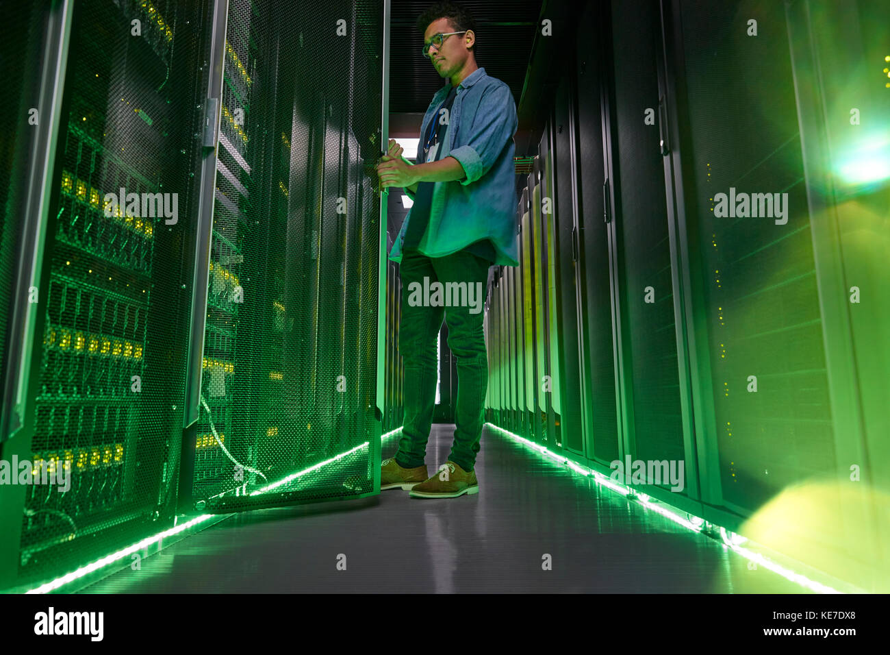 Male IT technician working in dark server room with glowing green ...