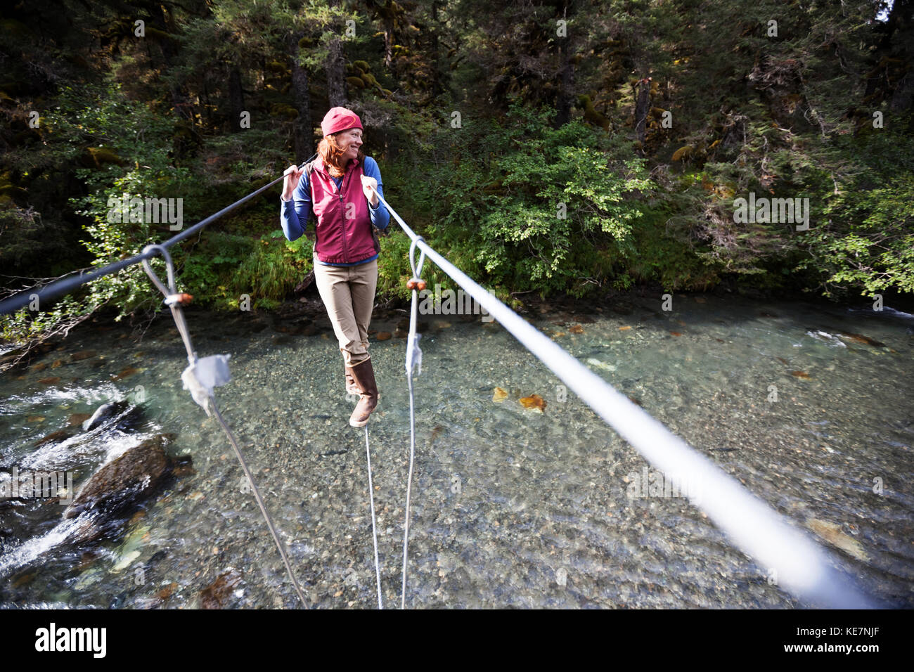 A Woman Walks On A Cable On A Suspension Bridge Over A River; Alaska ...