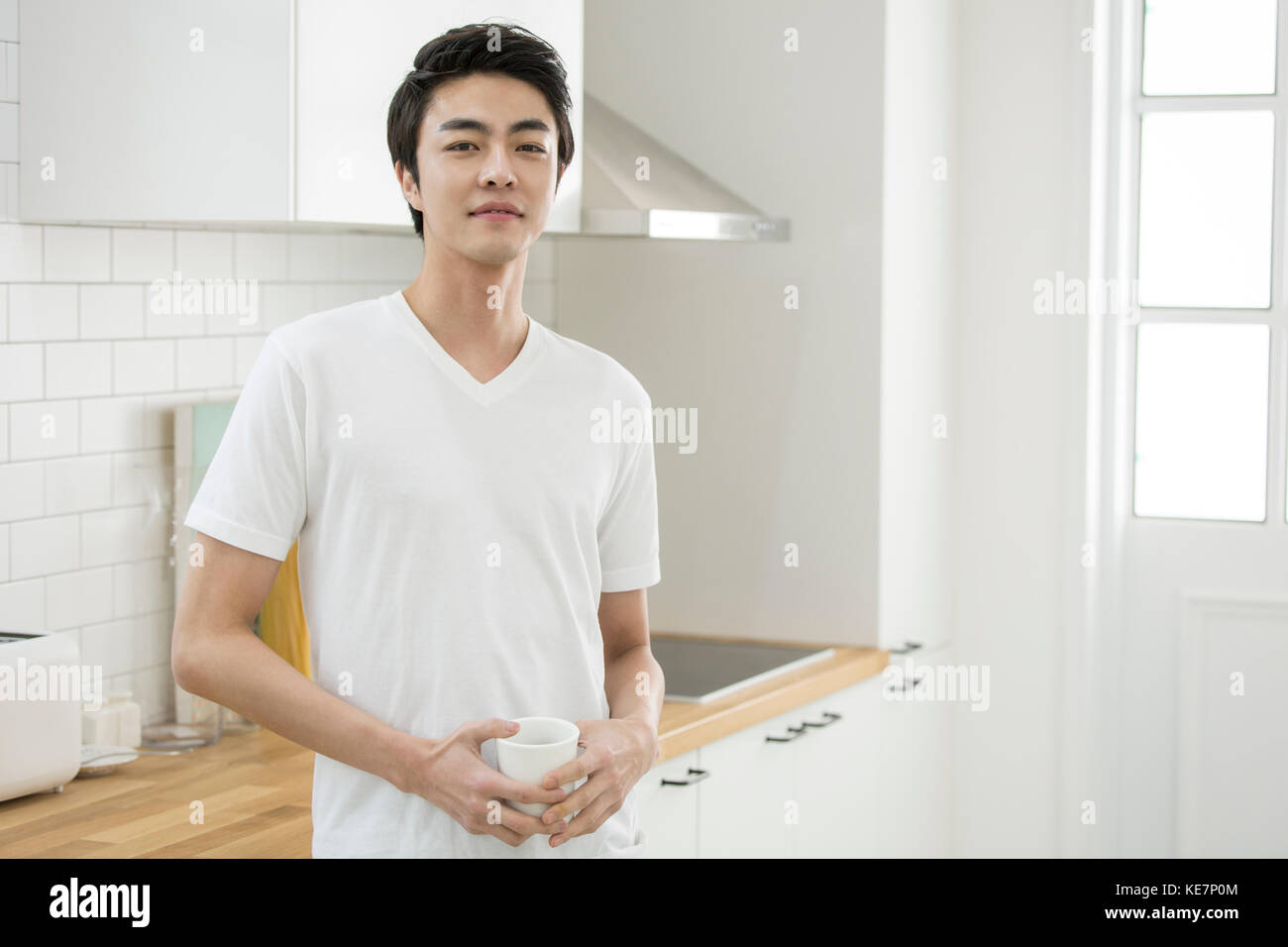 Smiling single man in white t-shirt holding a mug Stock Photo - Alamy