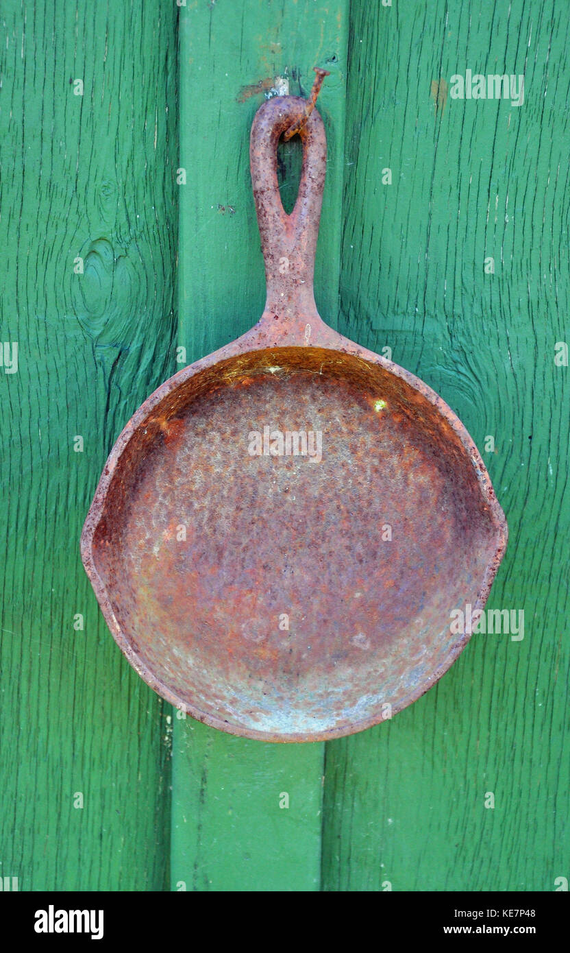Old rusty frying pan hanging on green wall of cabin Stock Photo - Alamy