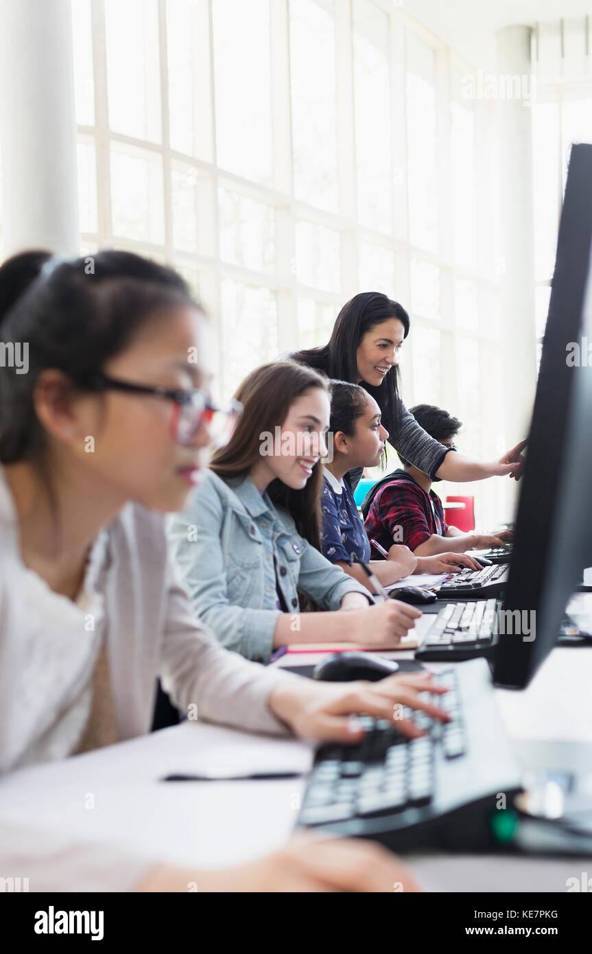 Female teacher helping students working at computers in computer lab ...
