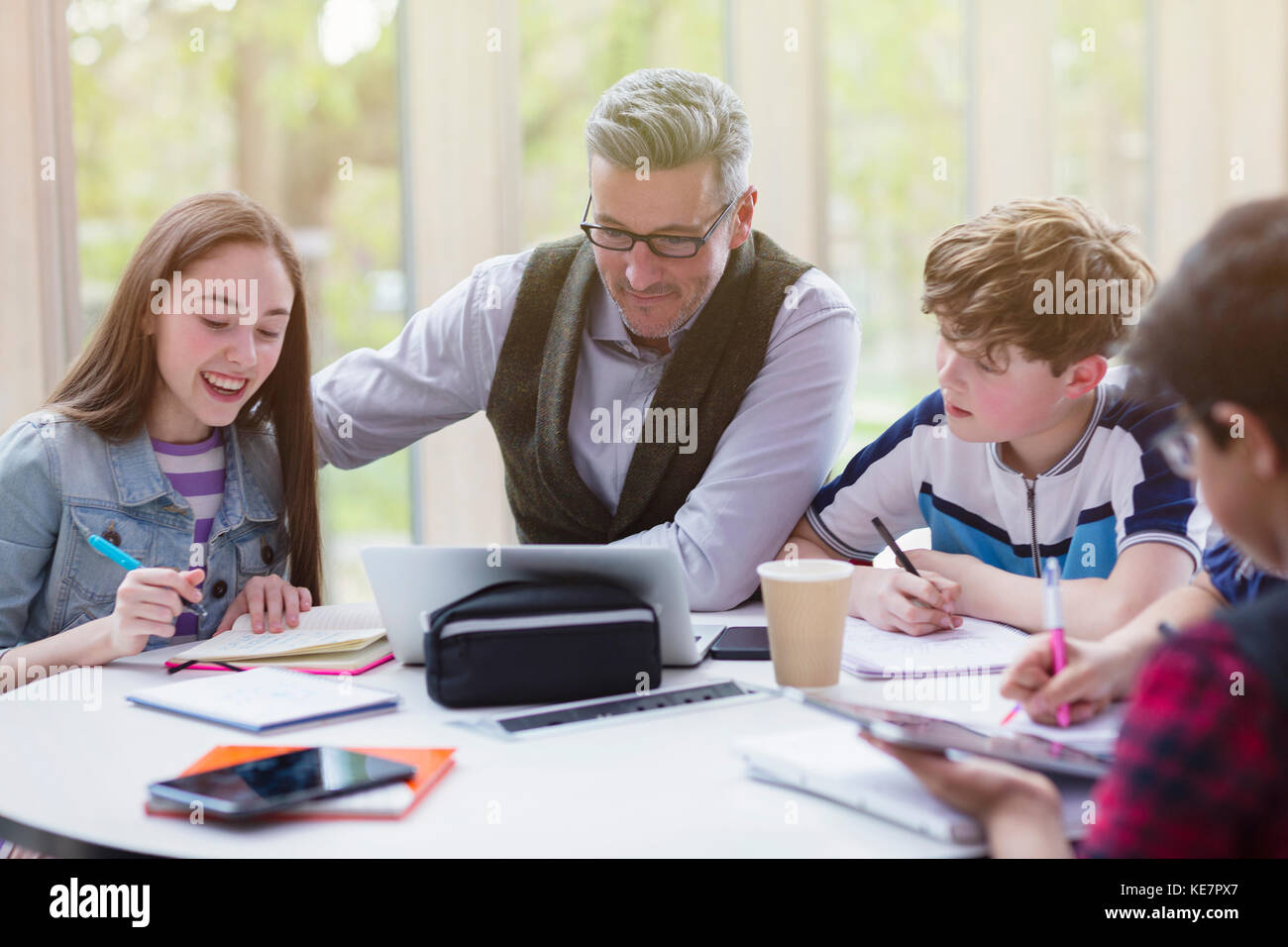 Male teacher and students researching at laptop in library Stock Photo ...