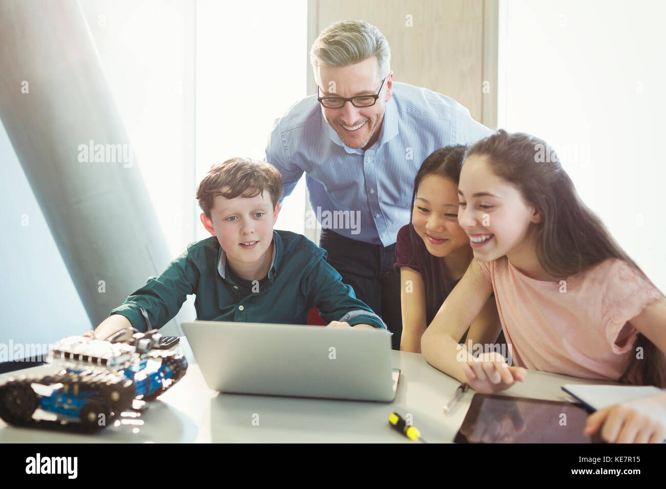 Smiling male teacher and students programming robotics at laptop in classroom Stock Photo - Alamy