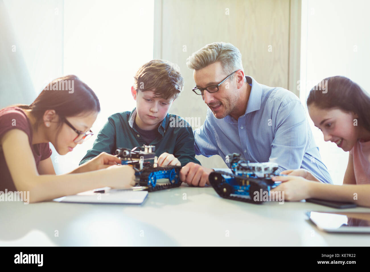 Male teacher helping students assembling robotics in classroom Stock ...