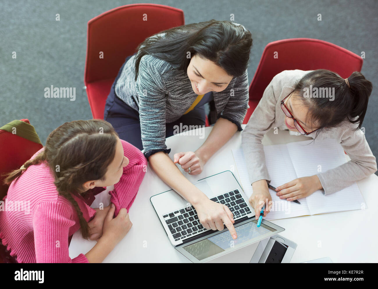 Female teacher helping girl students researching at laptop at library ...