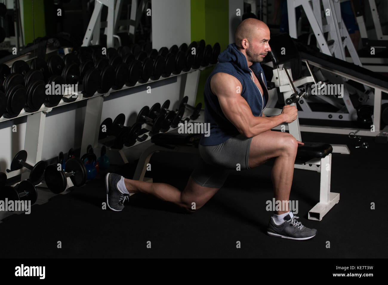 Muscular Man Stretching His Leg At The Floor In A Gym And Flexing ...