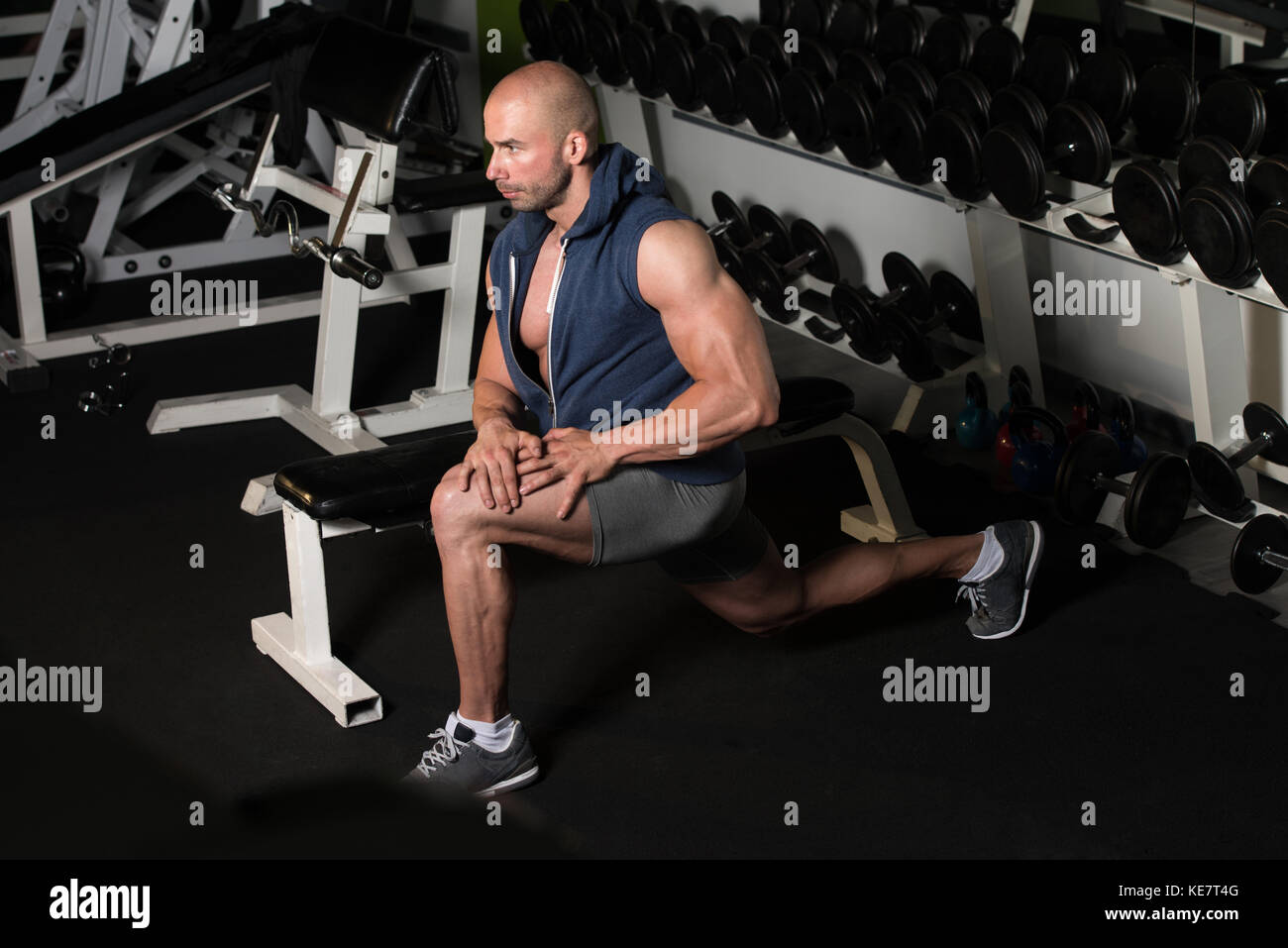 Muscular Man Stretching His Leg At The Floor In A Gym And Flexing ...