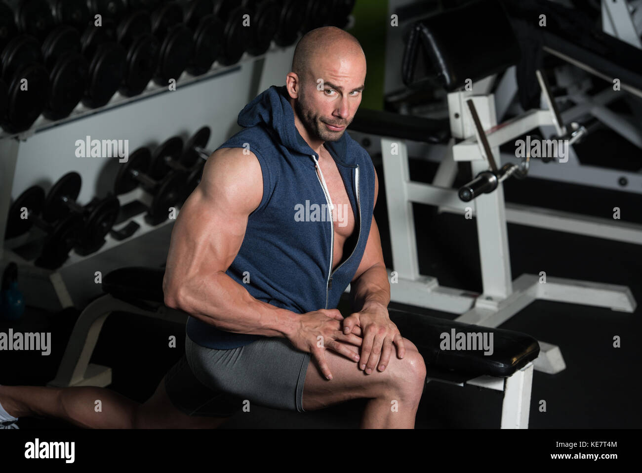 Muscular Man Stretching His Leg At The Floor In A Gym And Flexing ...